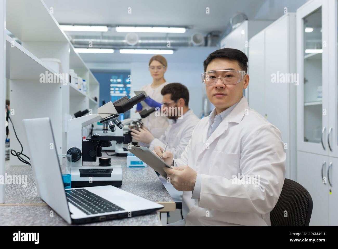 International group of young scientists work in the laboratory. An Asian man is sitting at a ...