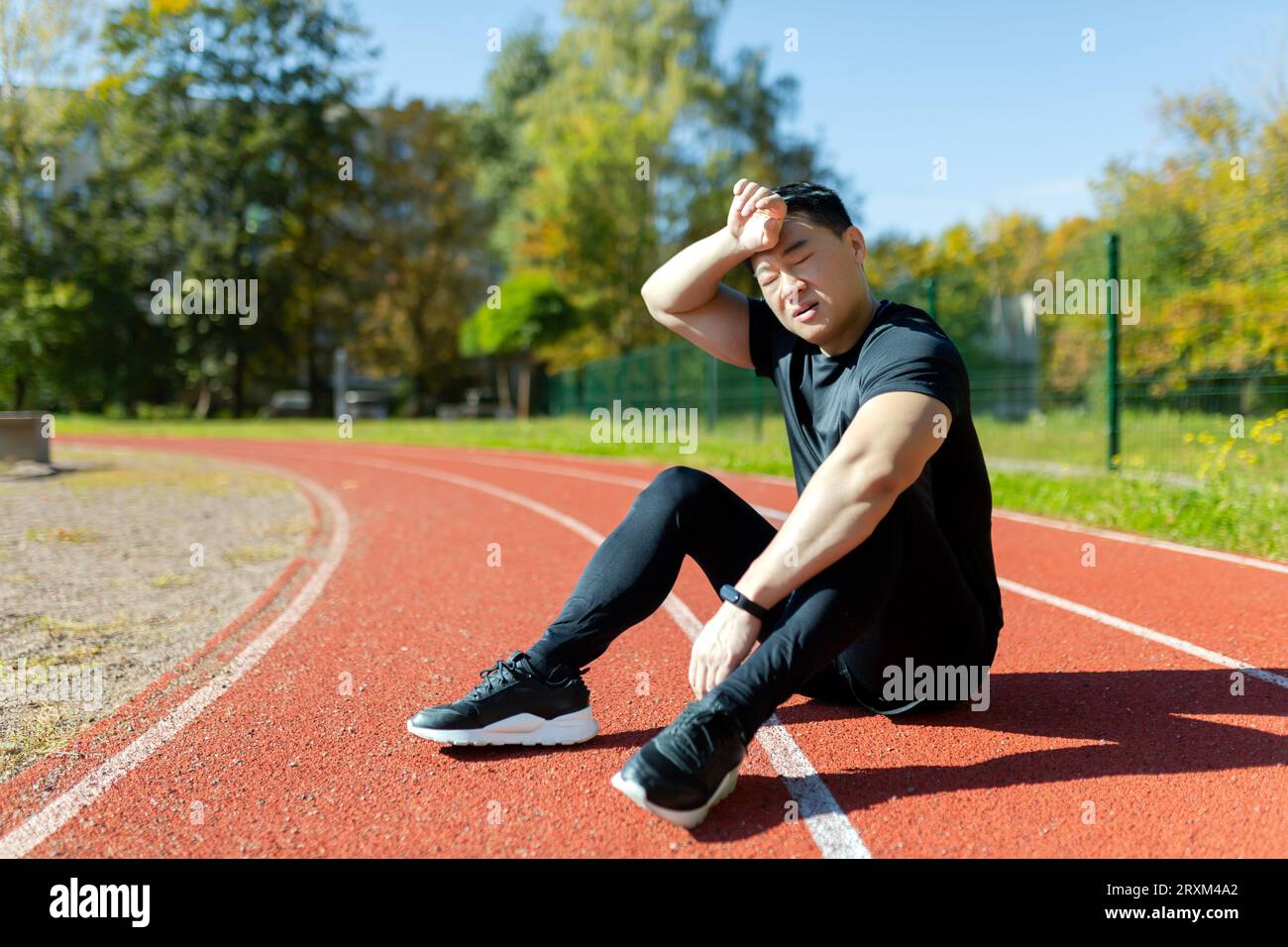 Tired young asian sportsman and runner sitting in stadium and wiping ...