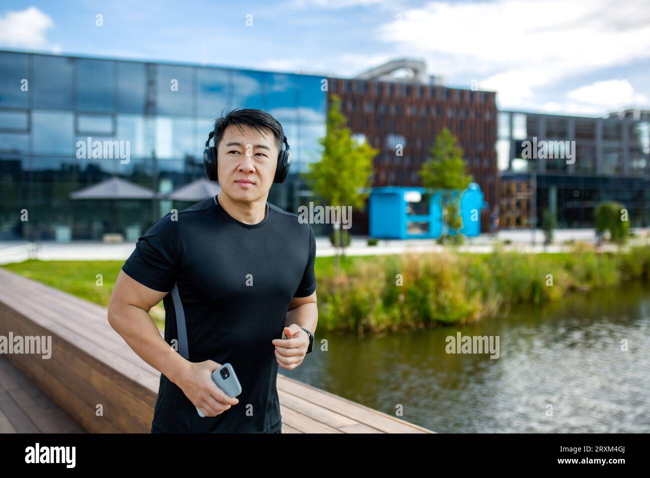 Serious young Asian sportsman man running in the park, exercising while ...