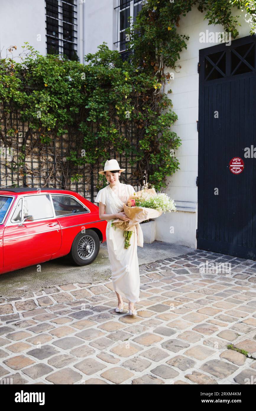 Woman wearing straw hat carrying flowers on driveway Stock Photo - Alamy