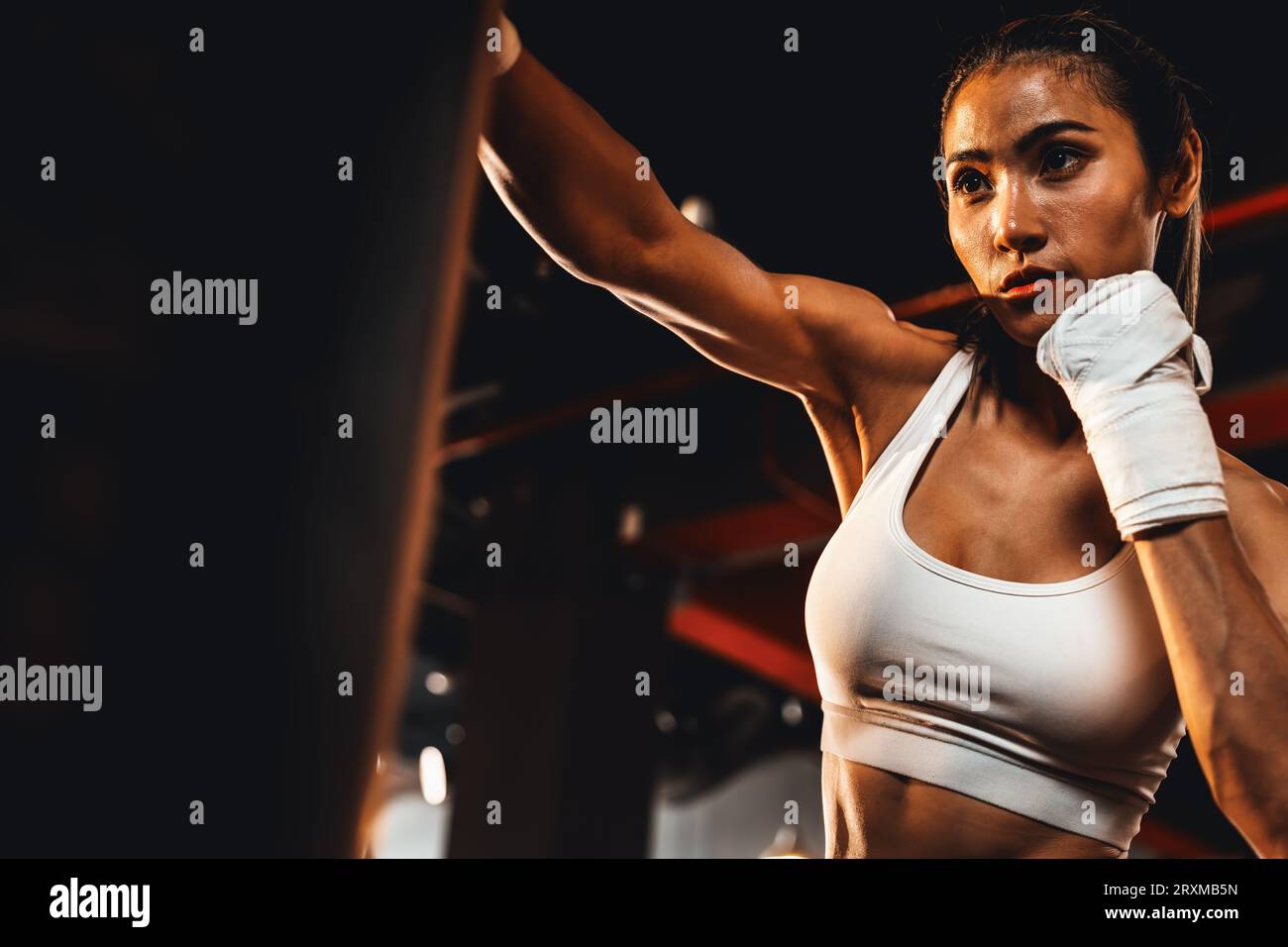 Asian female Muya Thai boxer training, wrapped hand punching at kicking ...