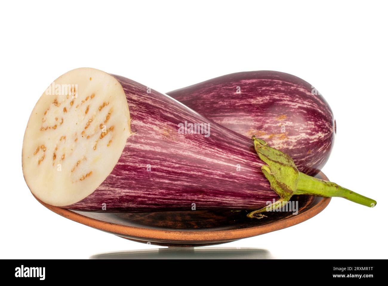 One whole and one half juicy eggplant on a clay plate, macro, isolated ...
