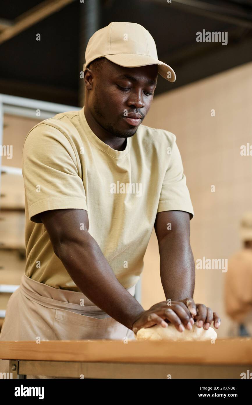 Vertical portrait of young Black man as baker kneading dough in artisan ...
