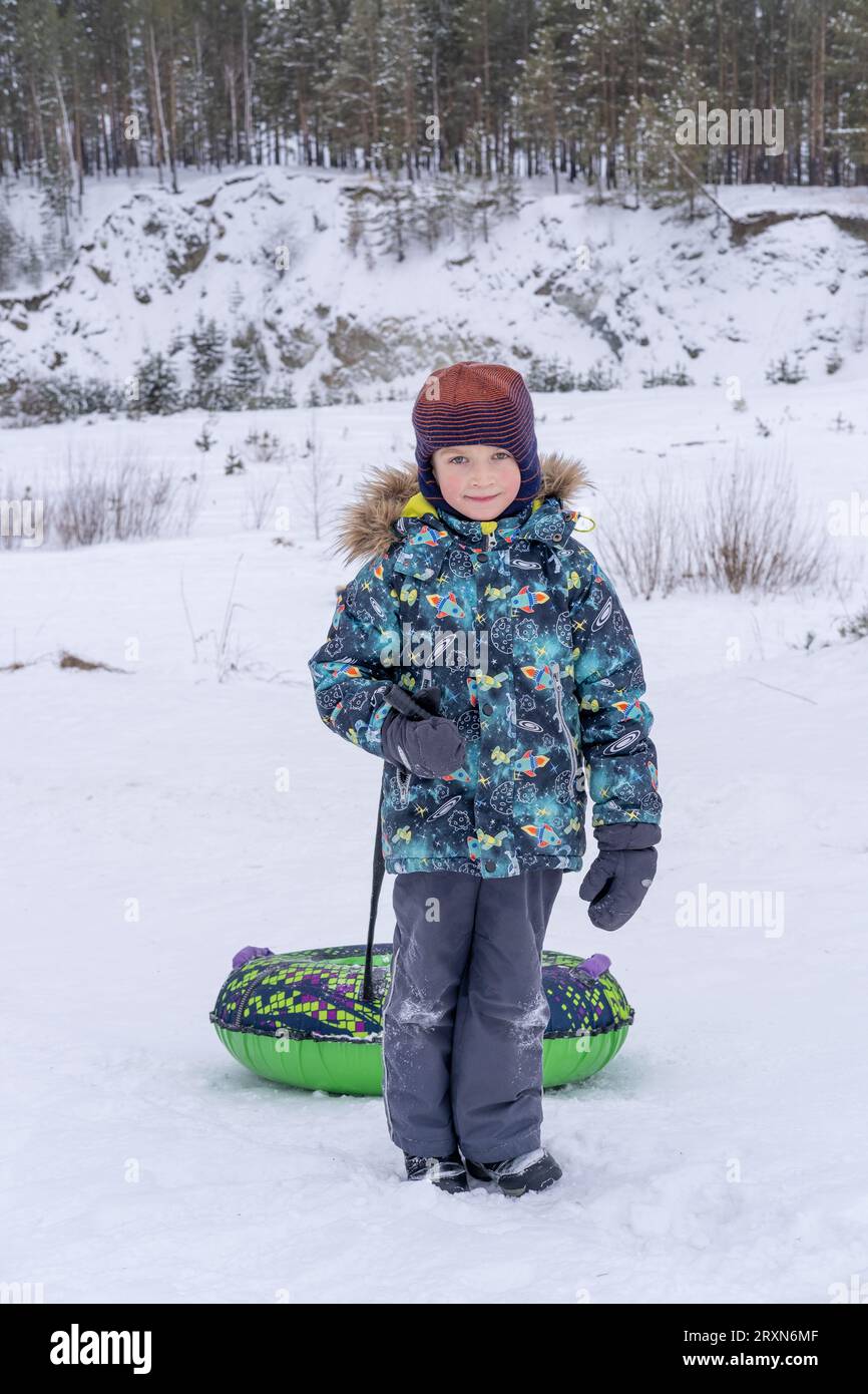 Happy smiling boy skating down a snowy hill on a sled. Winter outdoor ...