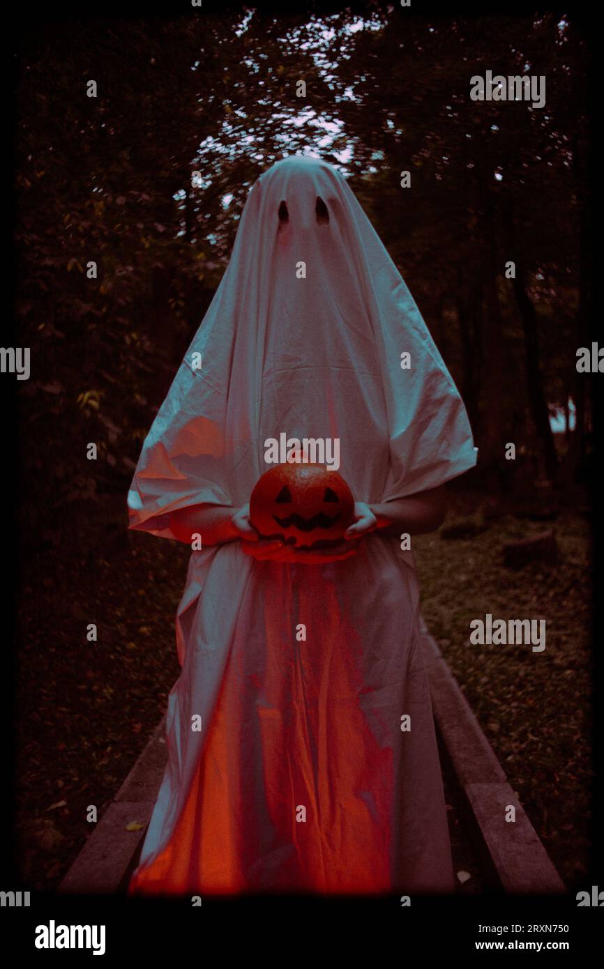 In the dimly lit autumn forest, a spooky ghost holds a jack's pumpkin ...