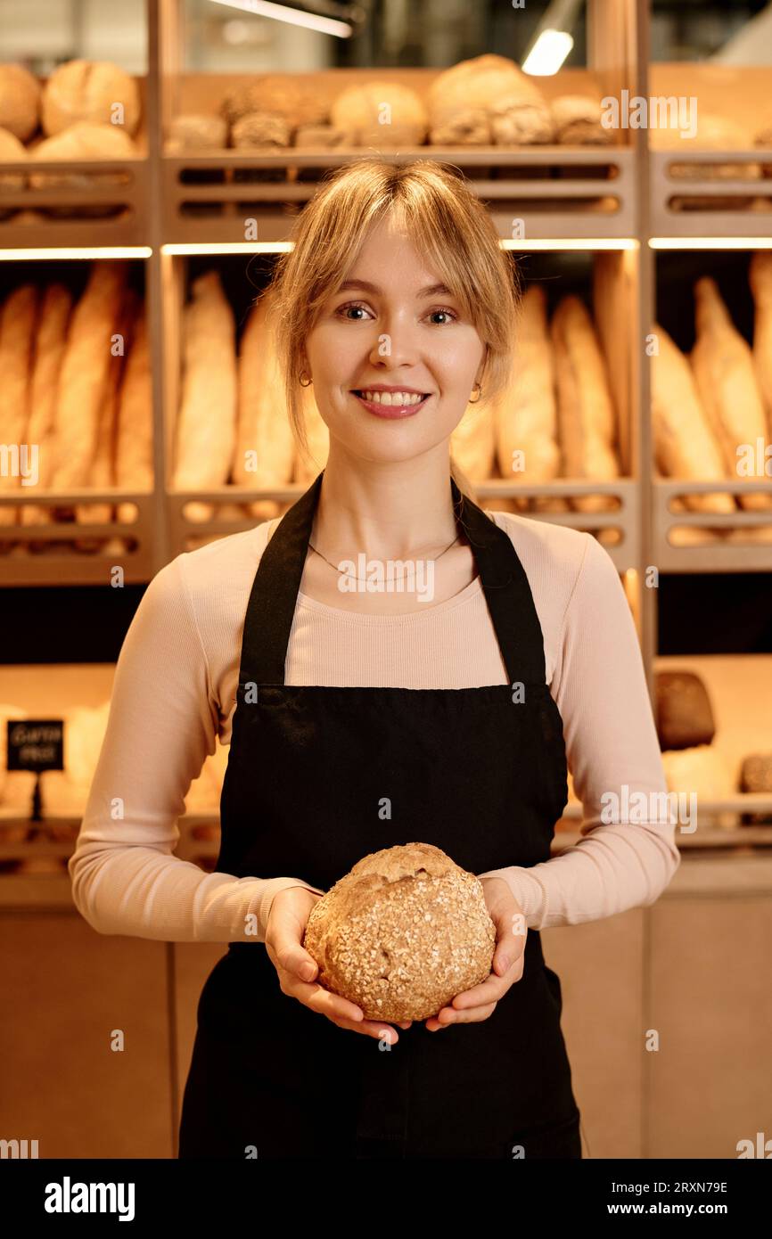 Vertical waist up portrait of smiling young woman holding fresh bread ...