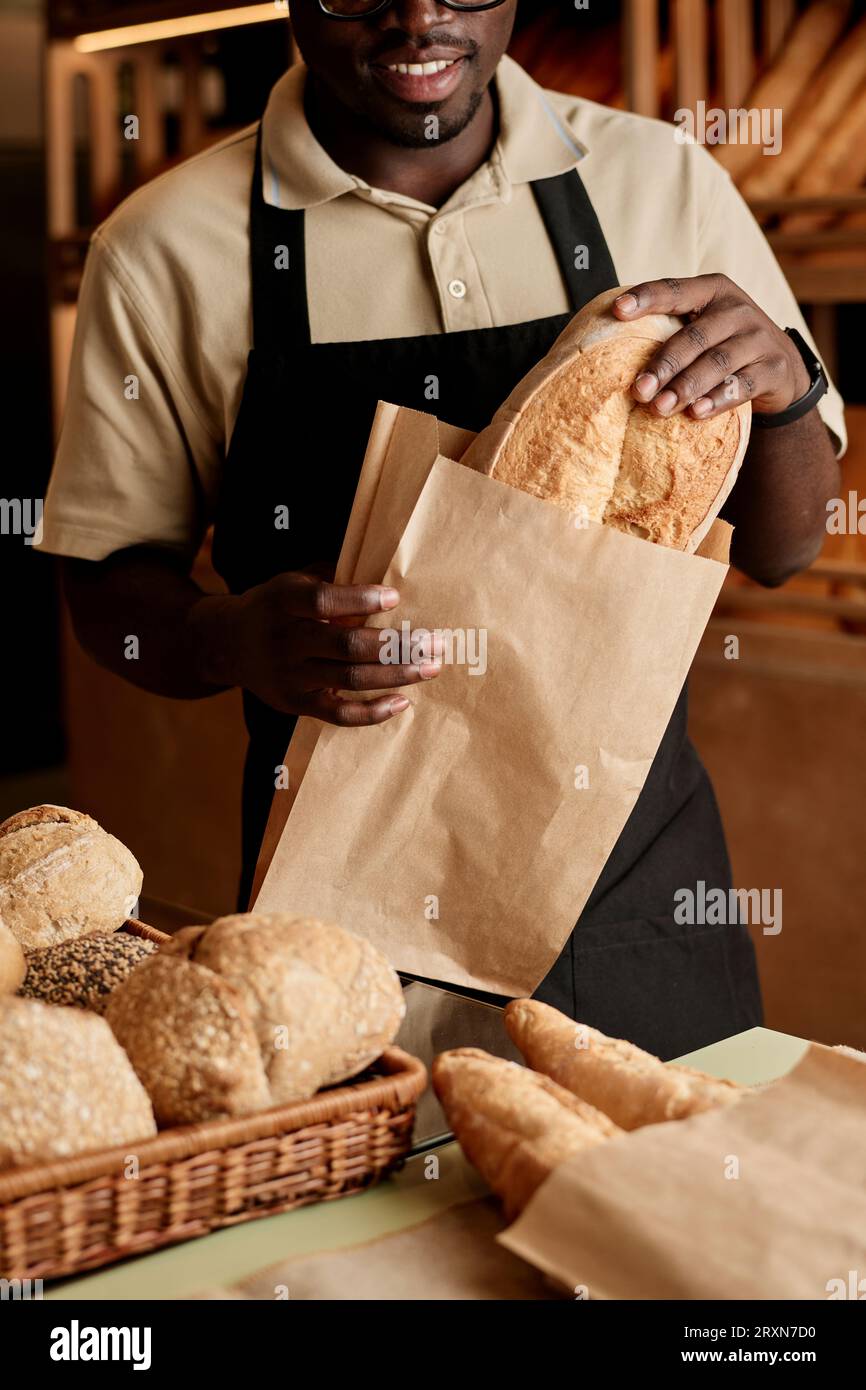 Vertical closeup of young man putting fresh bread in paper bag while ...