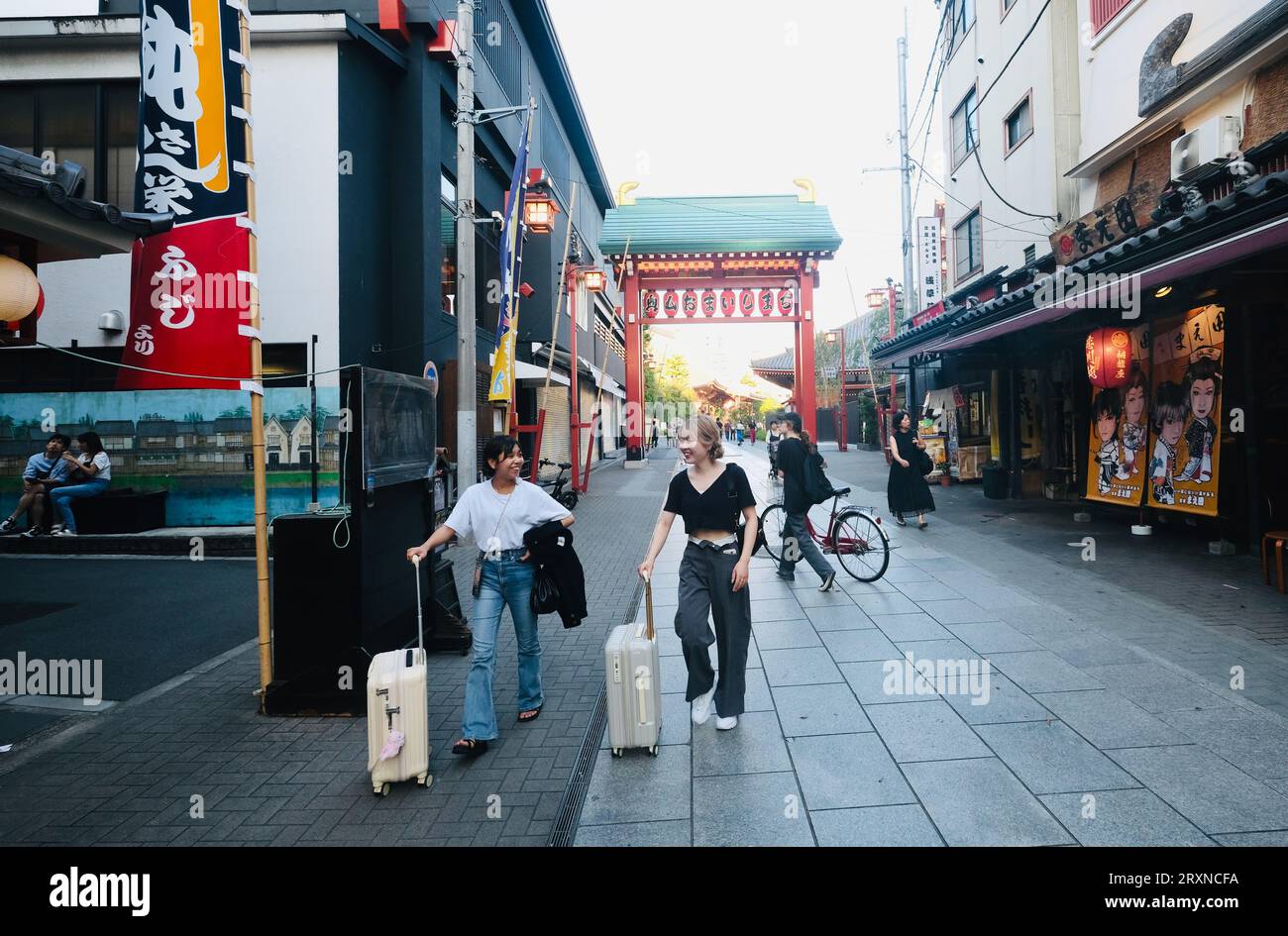 Two young Japanese women, pushing suitcases, walk along a backstreet in ...