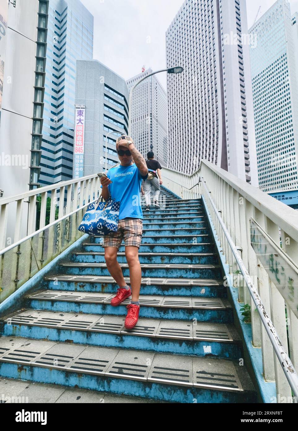 A man dressed in fashionable clothing walks down a pedestrian bridge in ...