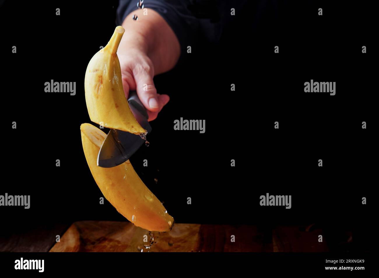 Woman cutting a banana in half with a knife in the air spilling water ...