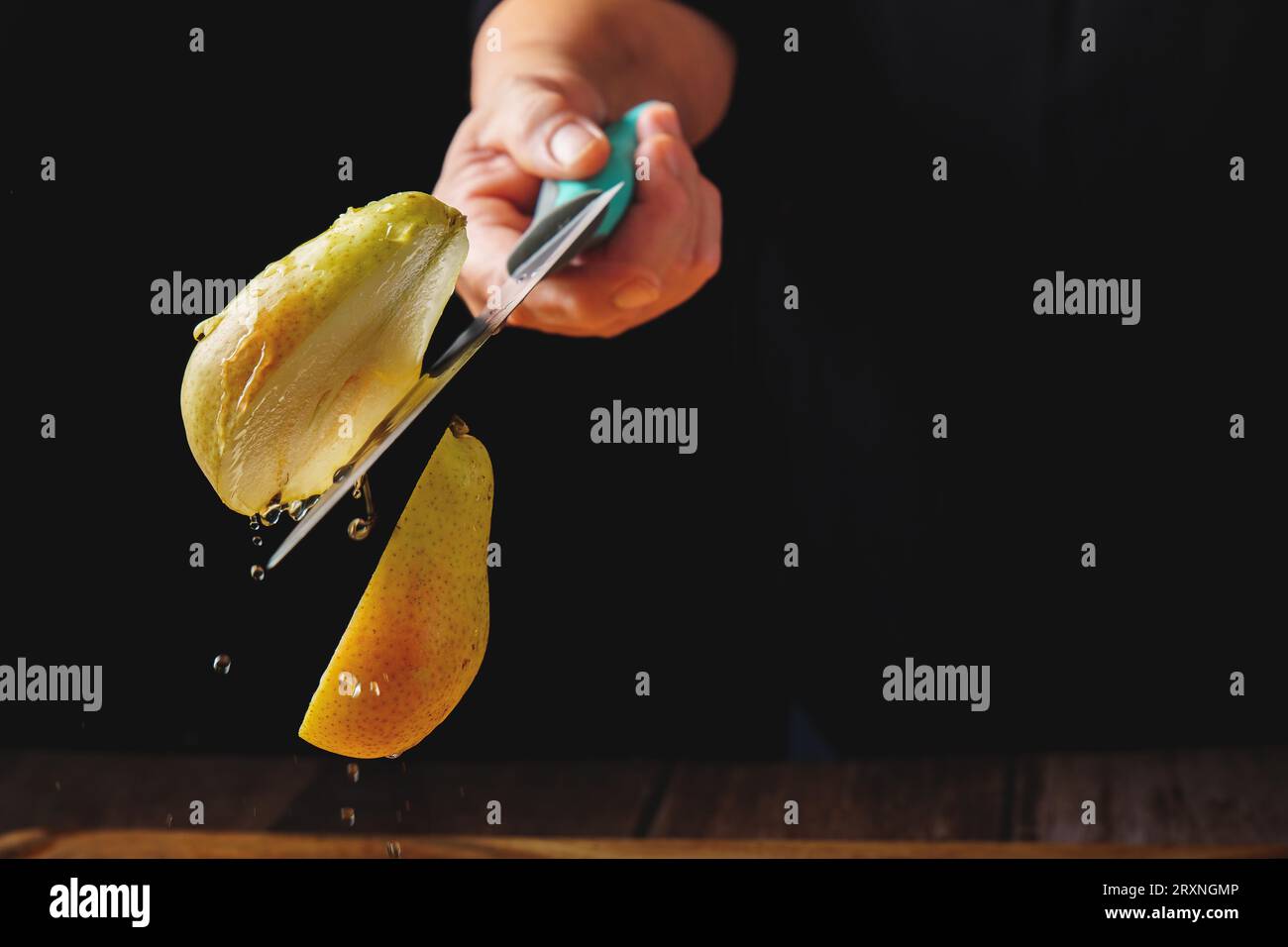 Woman cutting a pear in half with a knife in the air spilling water ...