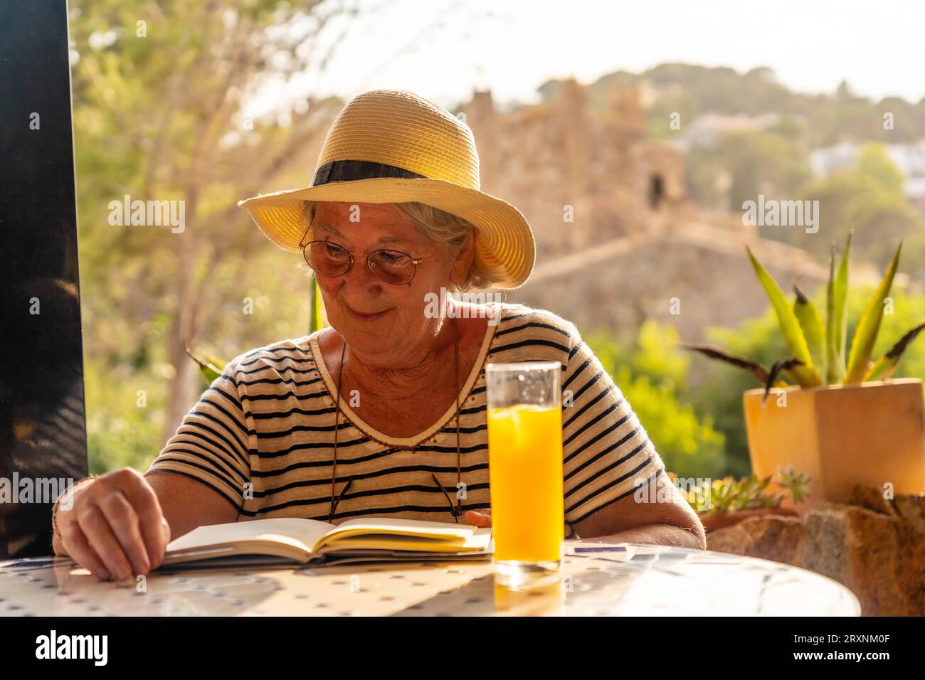 Happy elder woman reading a book in an outdoor terrace with views of ...