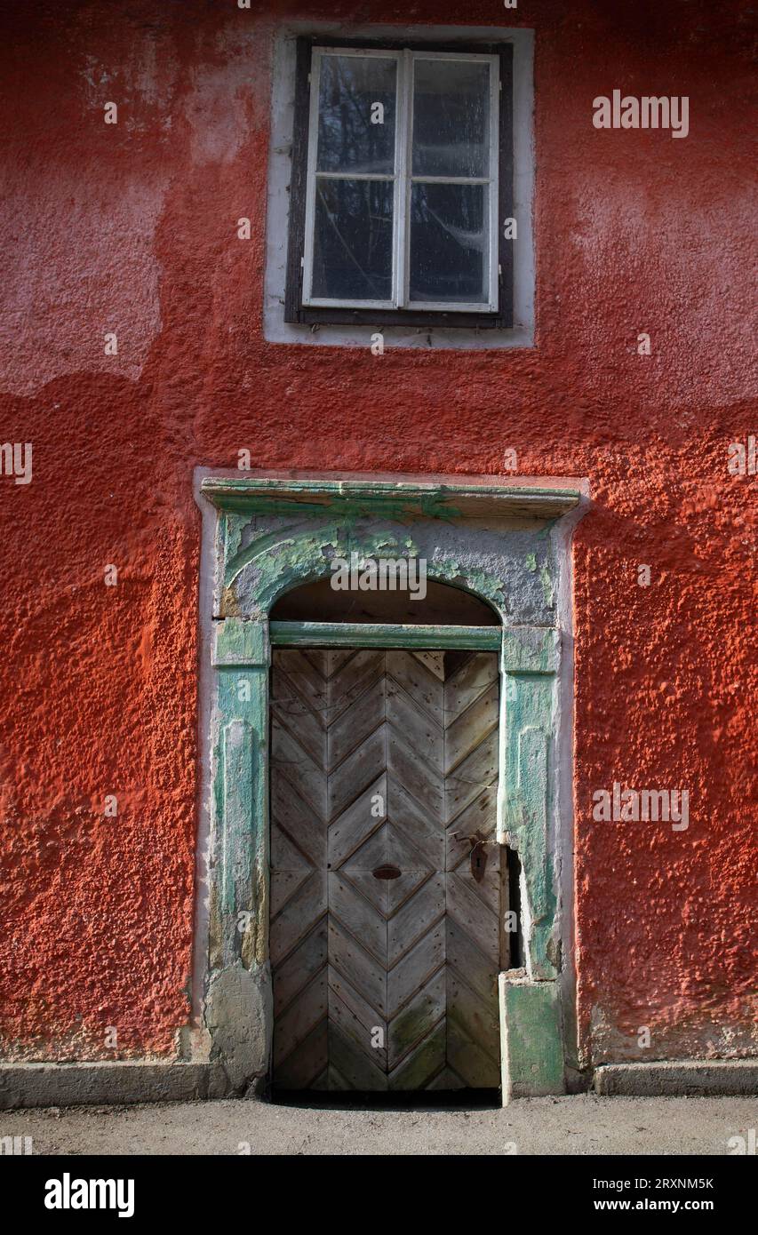Old red house wall with weathered windows and front door, masonry ...