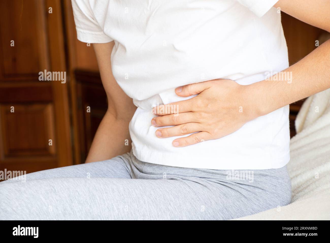 A girl sits on the bed with a sore stomach and holds her stomach, acute ...