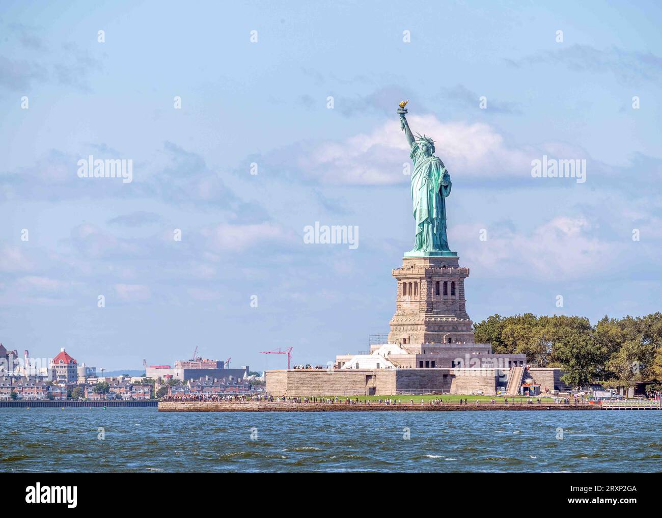 Statue of Liberty seen across water against blue sky with soft clouds ...