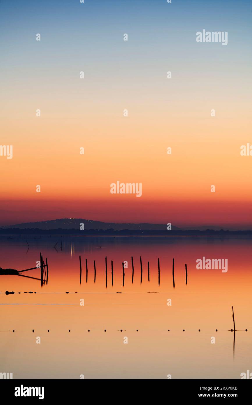 Sky over poles sticking out of Etang de lArnel pond at dusk, Herault ...