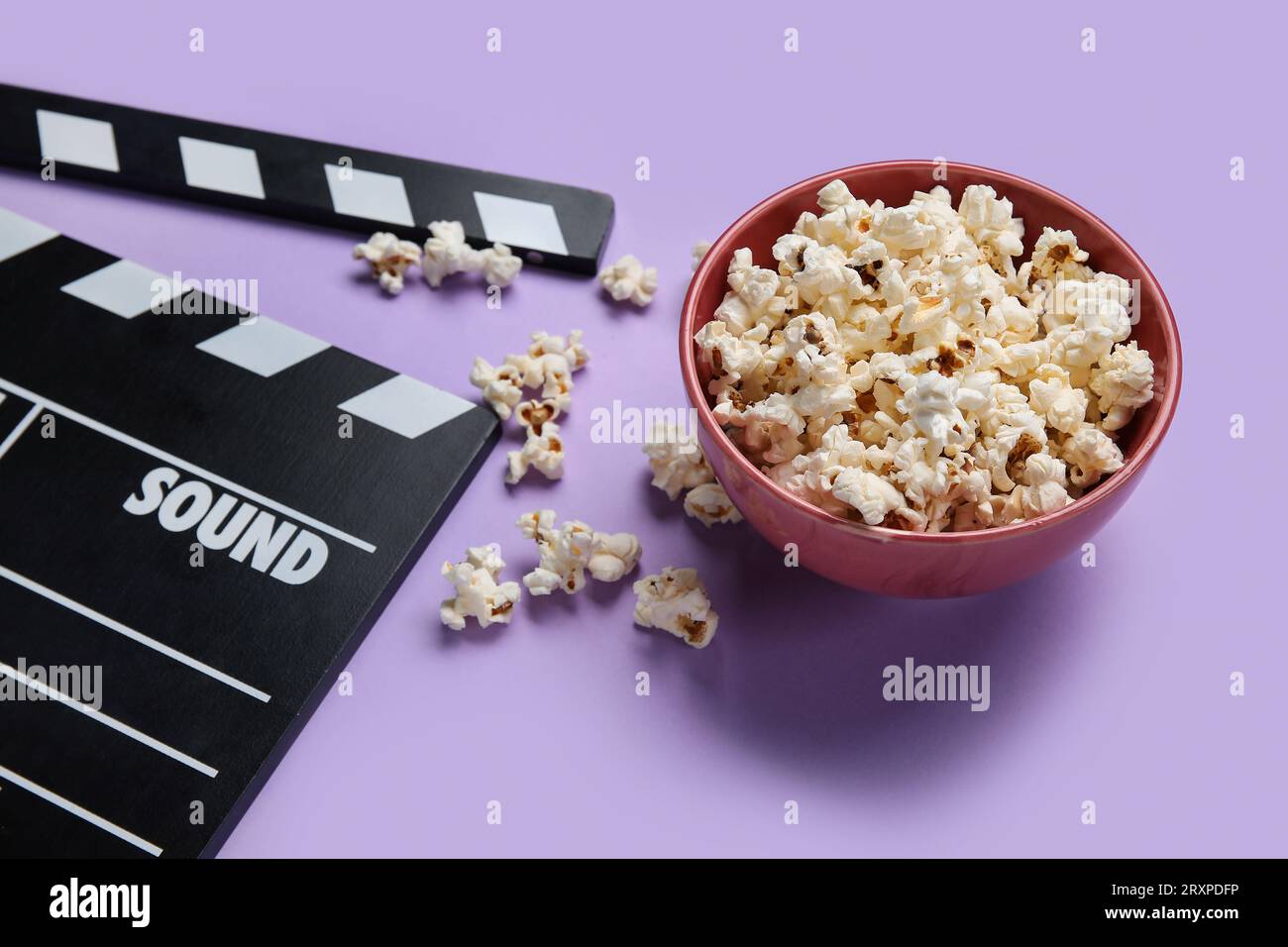 Bowl with tasty popcorn and clapperboard on purple background Stock ...