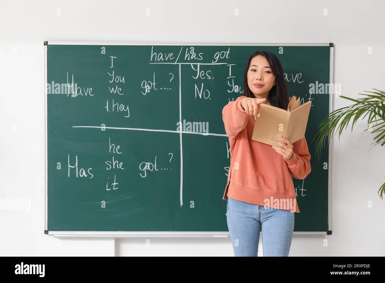 Female English teacher with book conducting grammar lesson in classroom ...