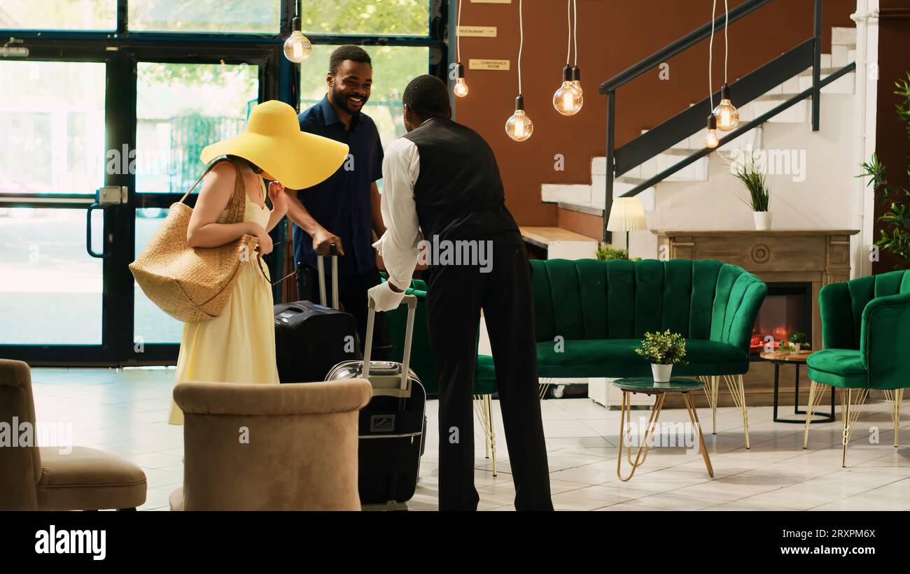 Hotel bellhop providing luxury service to guests entering reception lobby, concierge carrying ...