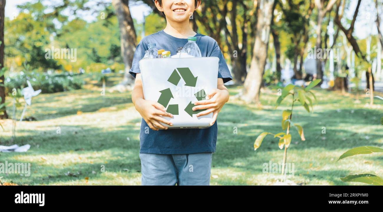 Cheerful young asian boy holding recycle symbol bin on daylight natural ...