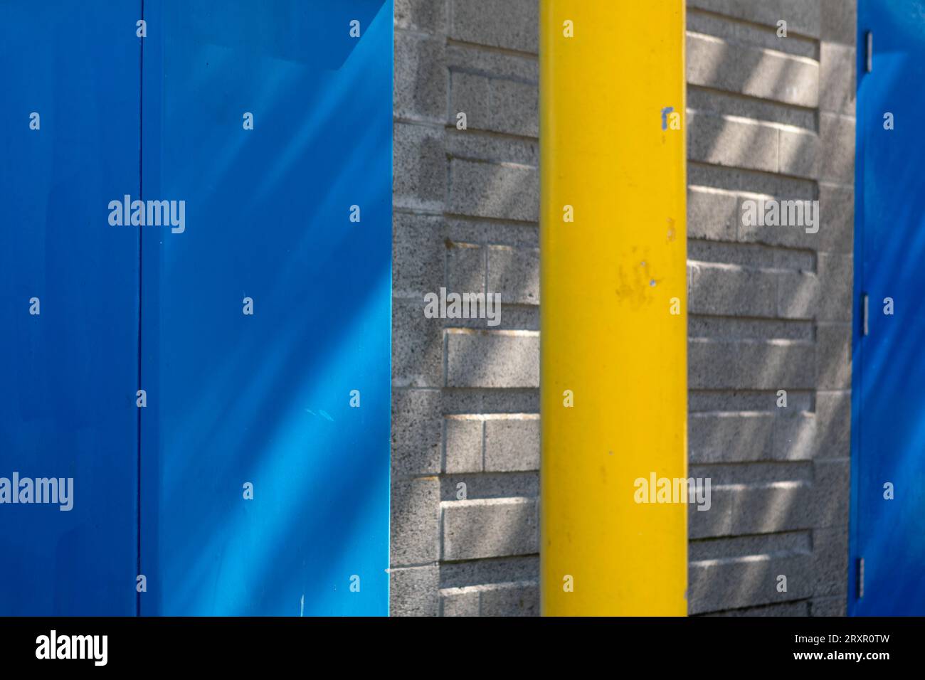 Closeup blue and yellow urban scene; sunlit blue wall, yellow pole ...