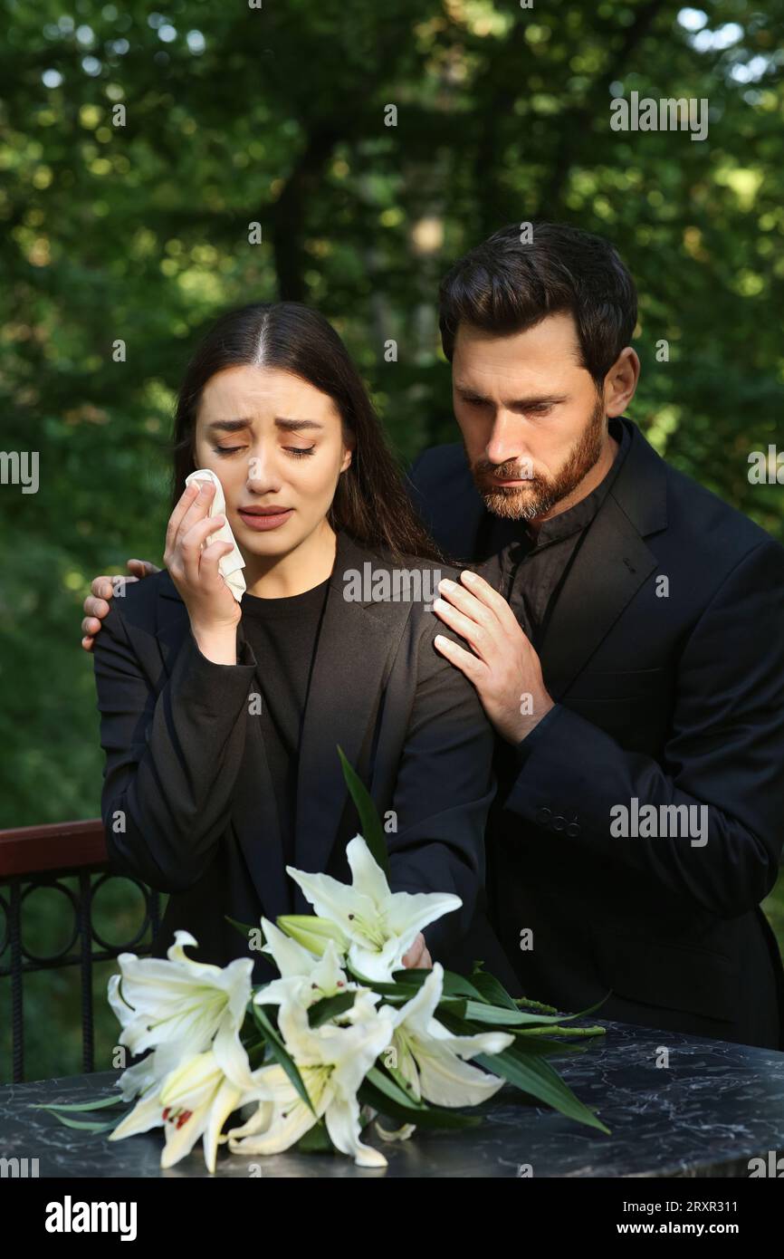 Sad couple mourning near granite tombstone with white lilies at ...