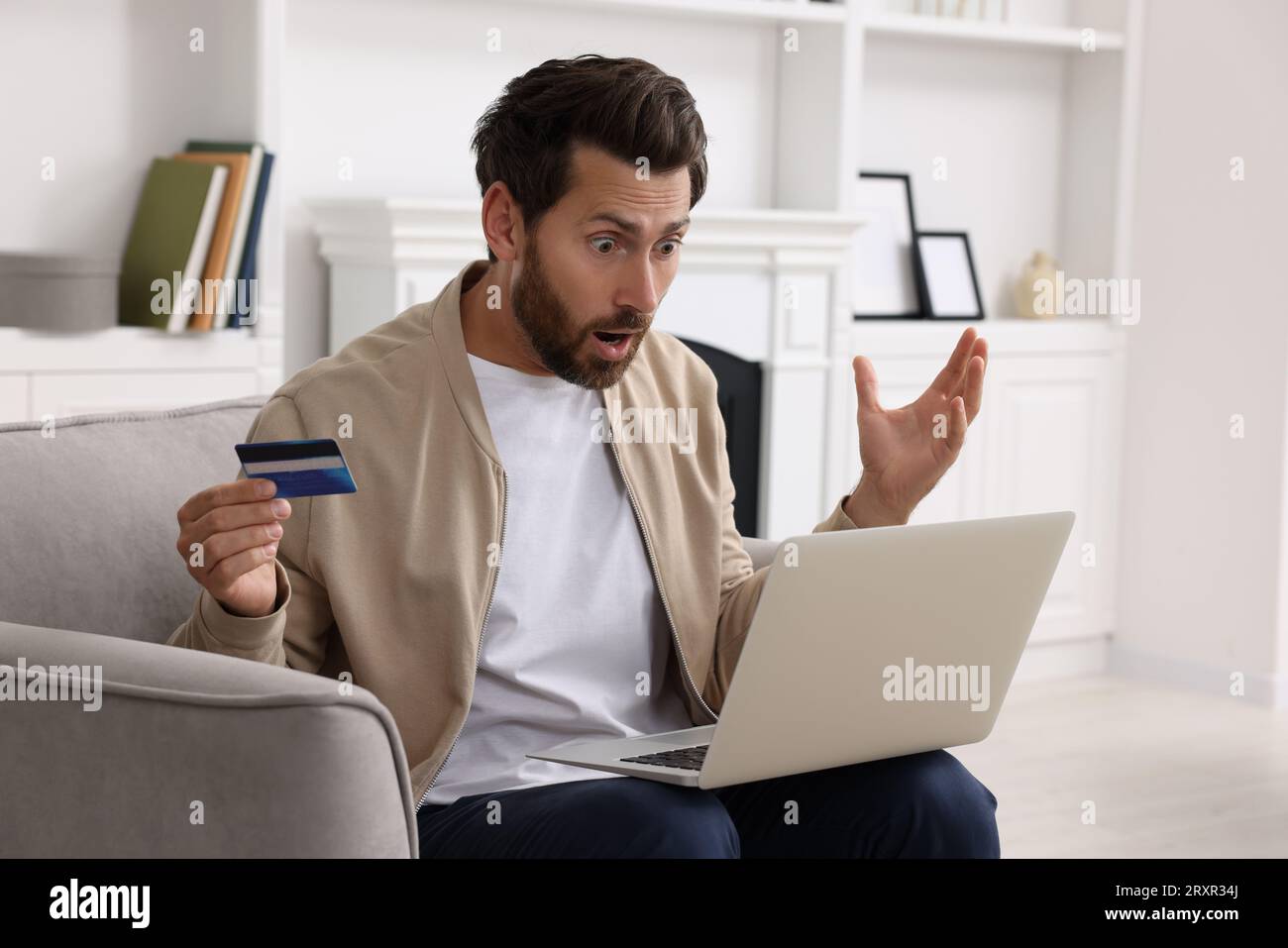 Shocked man with laptop and credit card in armchair at home. Be careful ...