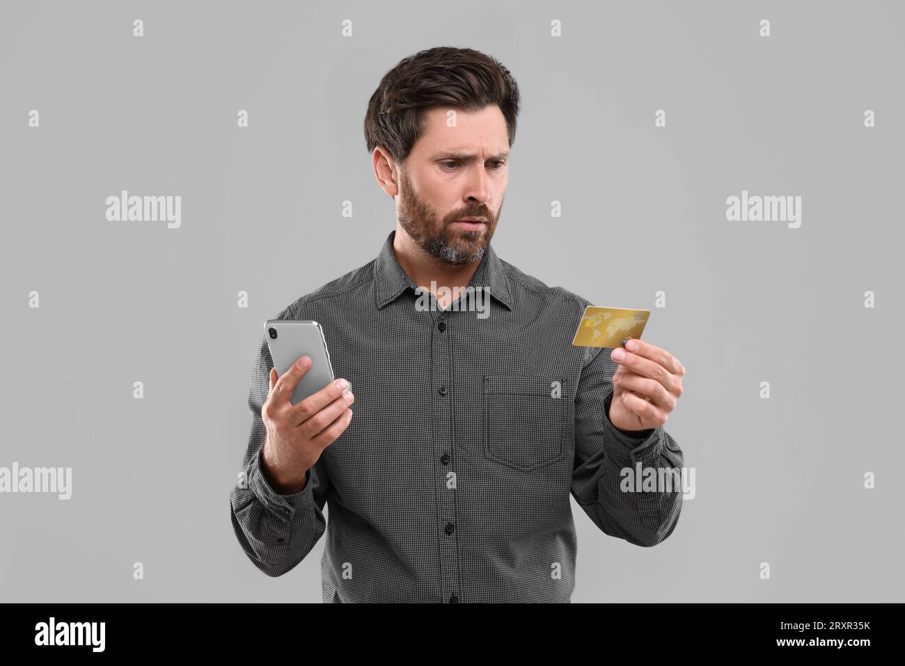 Emotional man holding smartphone and credit card on light grey ...