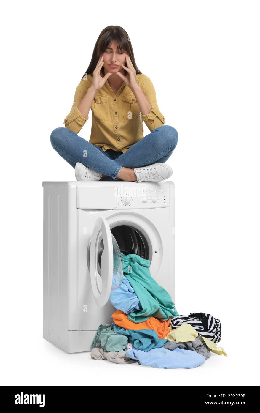 Confused woman sitting on washing machine with scattered laundry ...