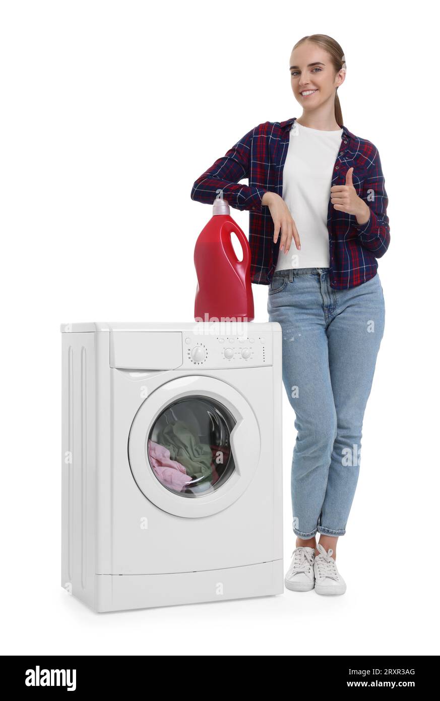 Beautiful young woman with detergent showing thumbs up near washing machine on white background ...