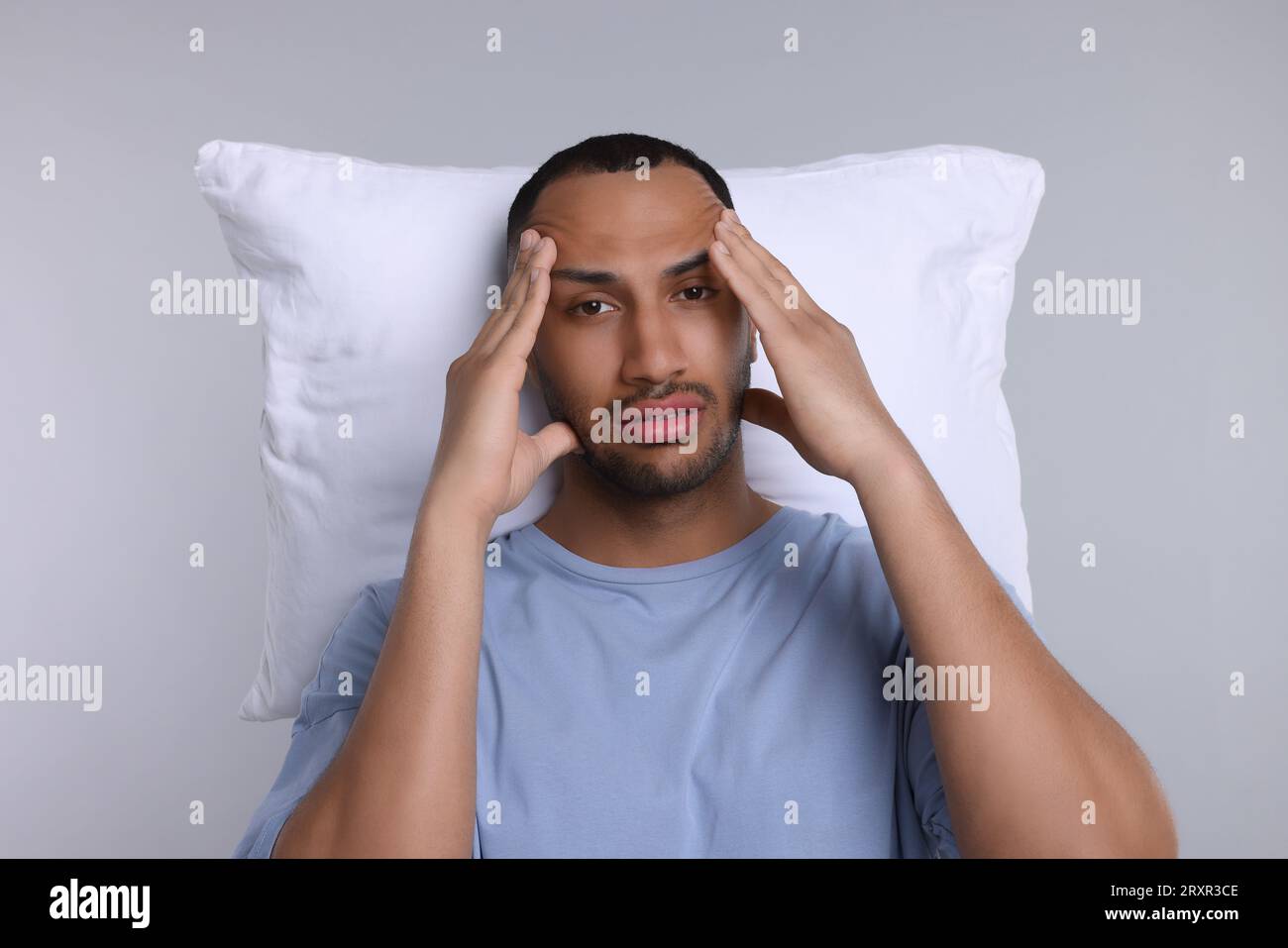 Tired man with pillow on light grey background. Insomnia problem Stock ...