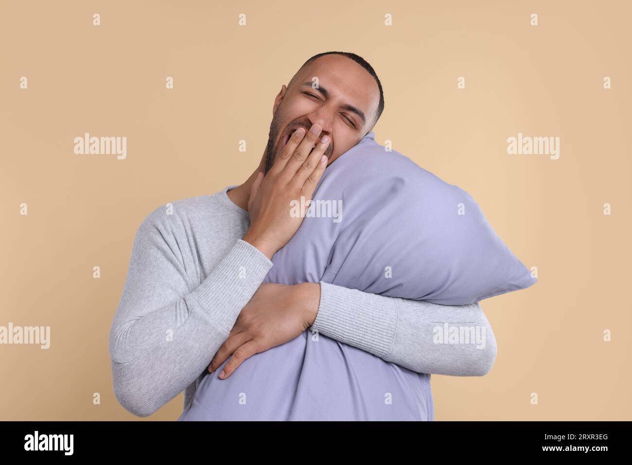 Sleepy man with pillow yawning on beige background. Insomnia problem ...