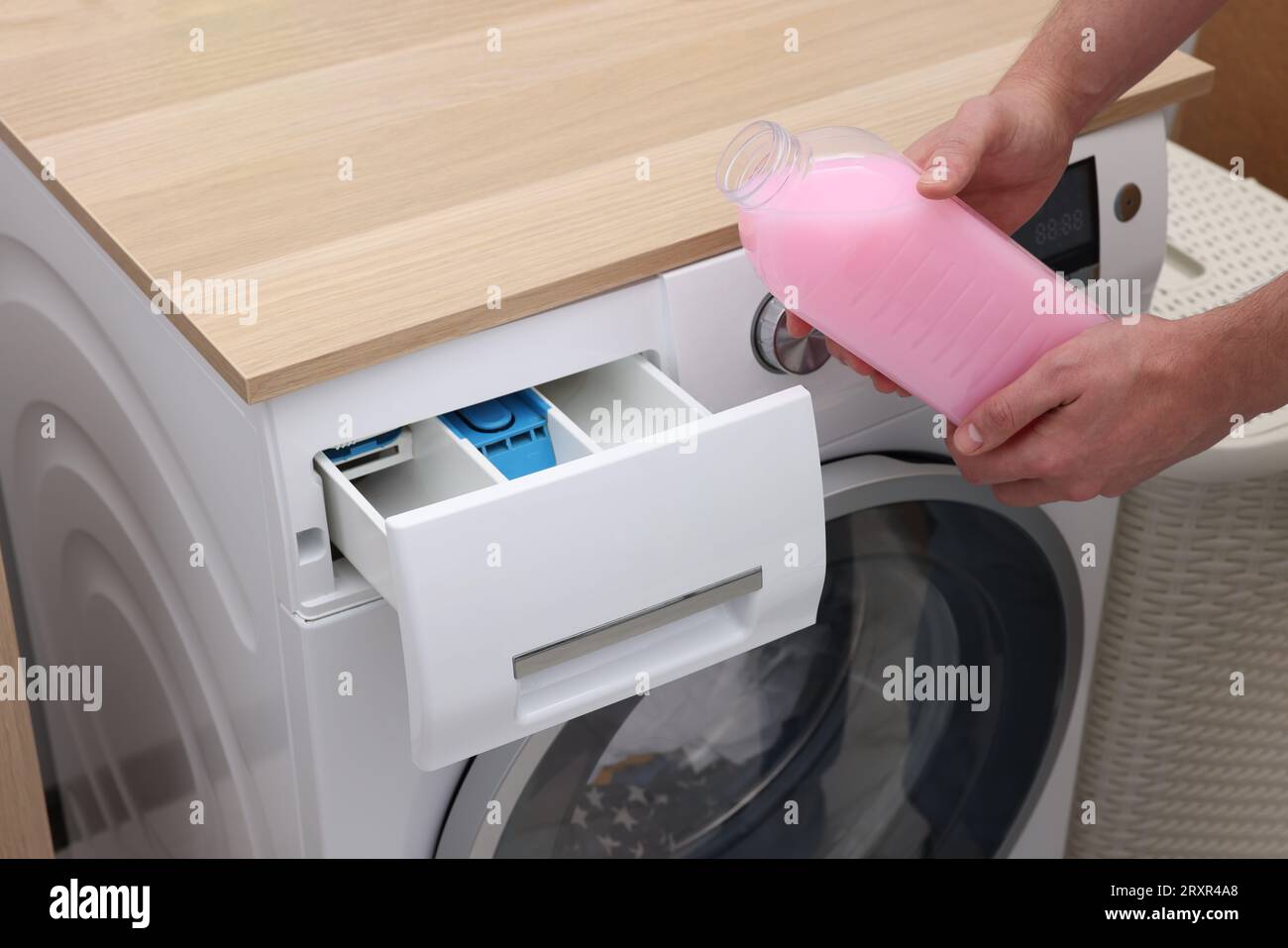 Man pouring fabric softener from bottle into washing machine indoors ...