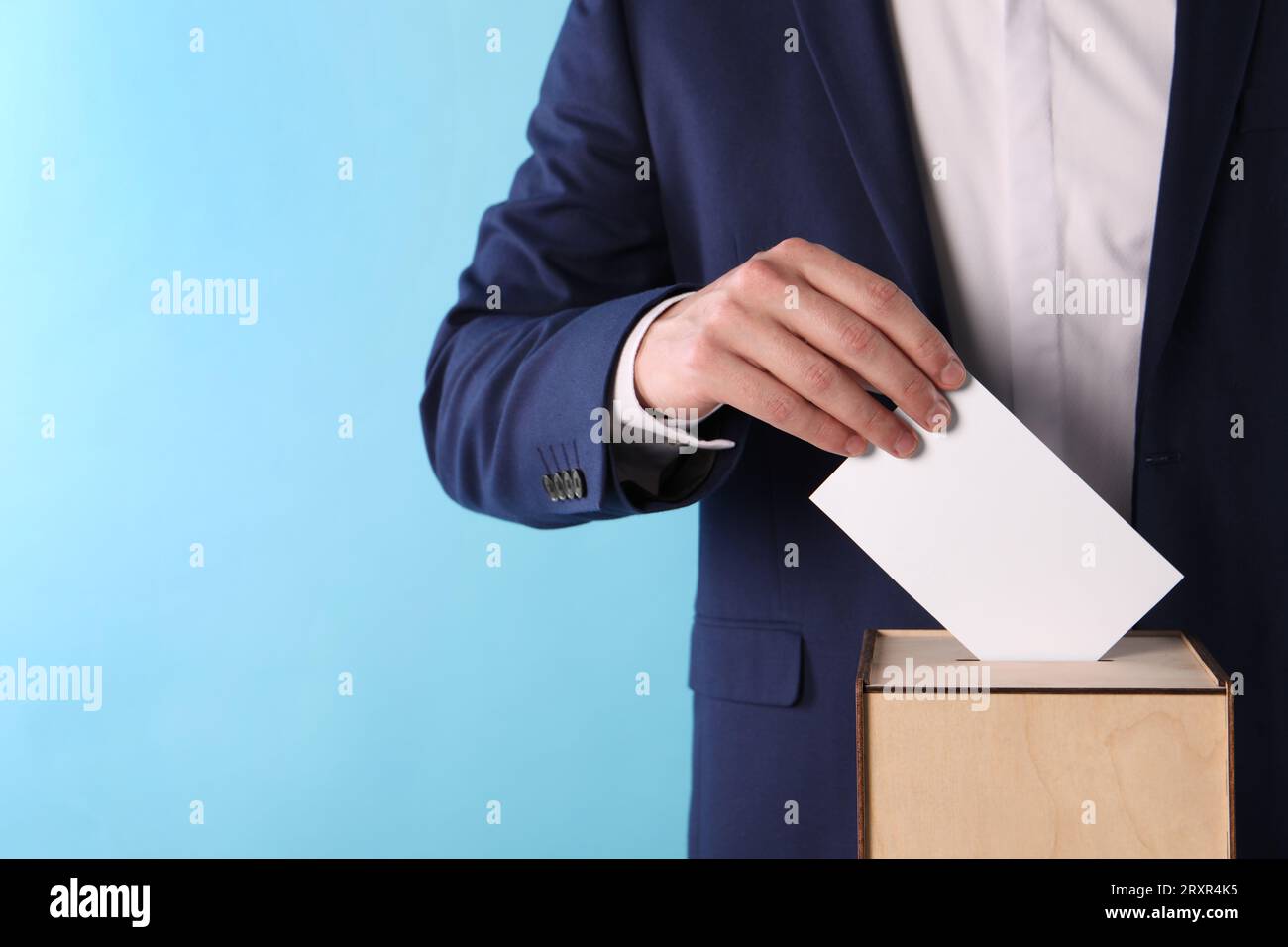 Man putting his vote into ballot box on light blue background, closeup ...