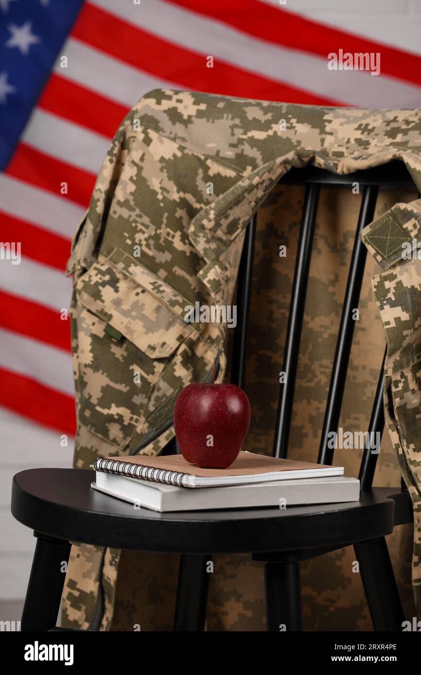 Soldier uniform, notebooks and apple on chair near flag of United ...