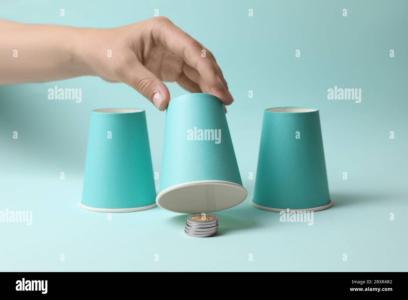 Woman showing coins under cup on light blue background, closeup ...
