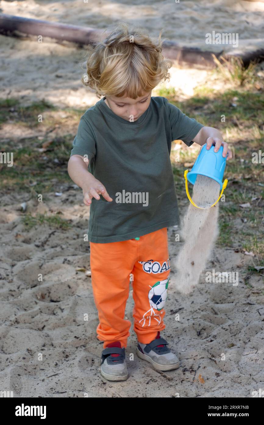 A little boy pours sand from a bucket on a sandpit Stock Photo - Alamy