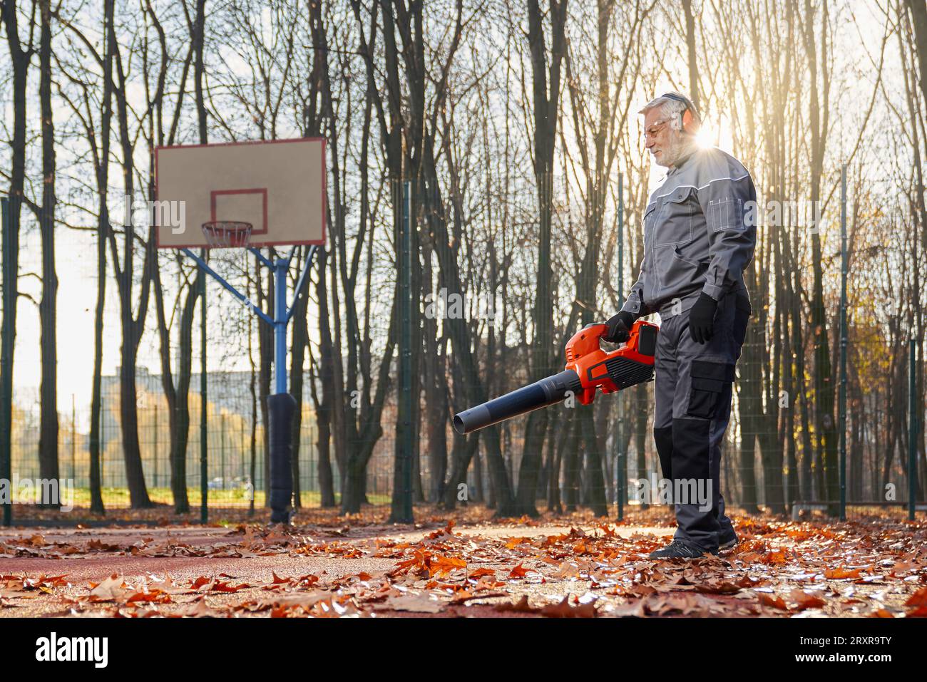 Smiling janitor with grey hair cleaning autumn city park with leaf ...