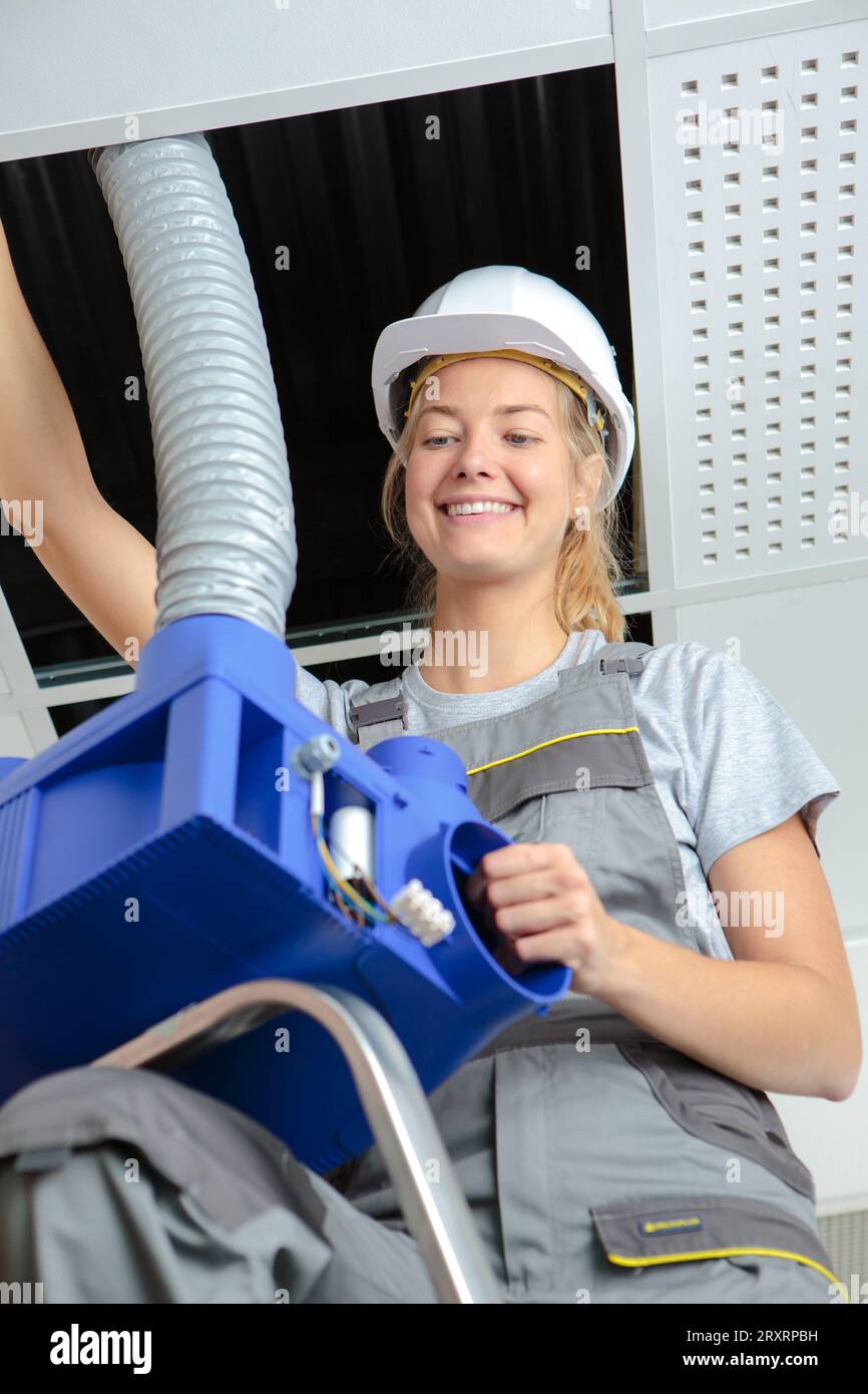 happy female worker fitting ventilation system in buildings ceiling ...