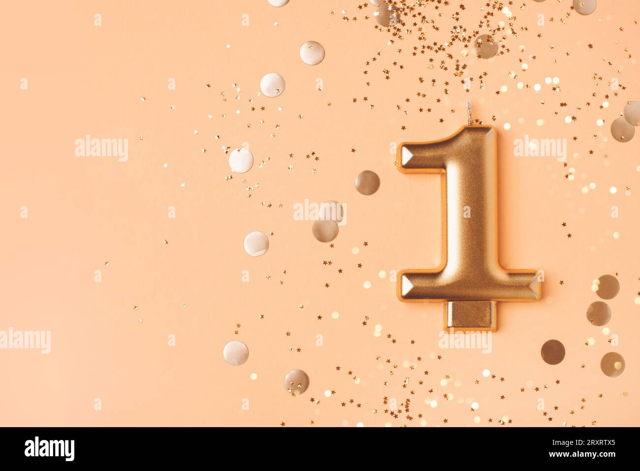 Gold candle in the form of number one on peach background with confetti ...
