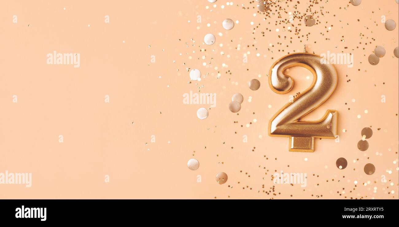 Gold candle in the form of number two peach background with confetti ...