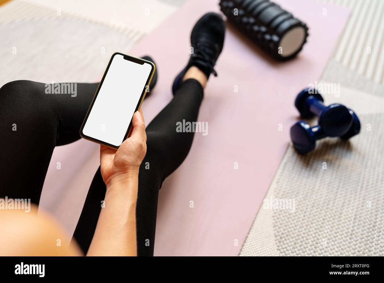 Female sports person sits on yoga mat and holding smart phone with ...