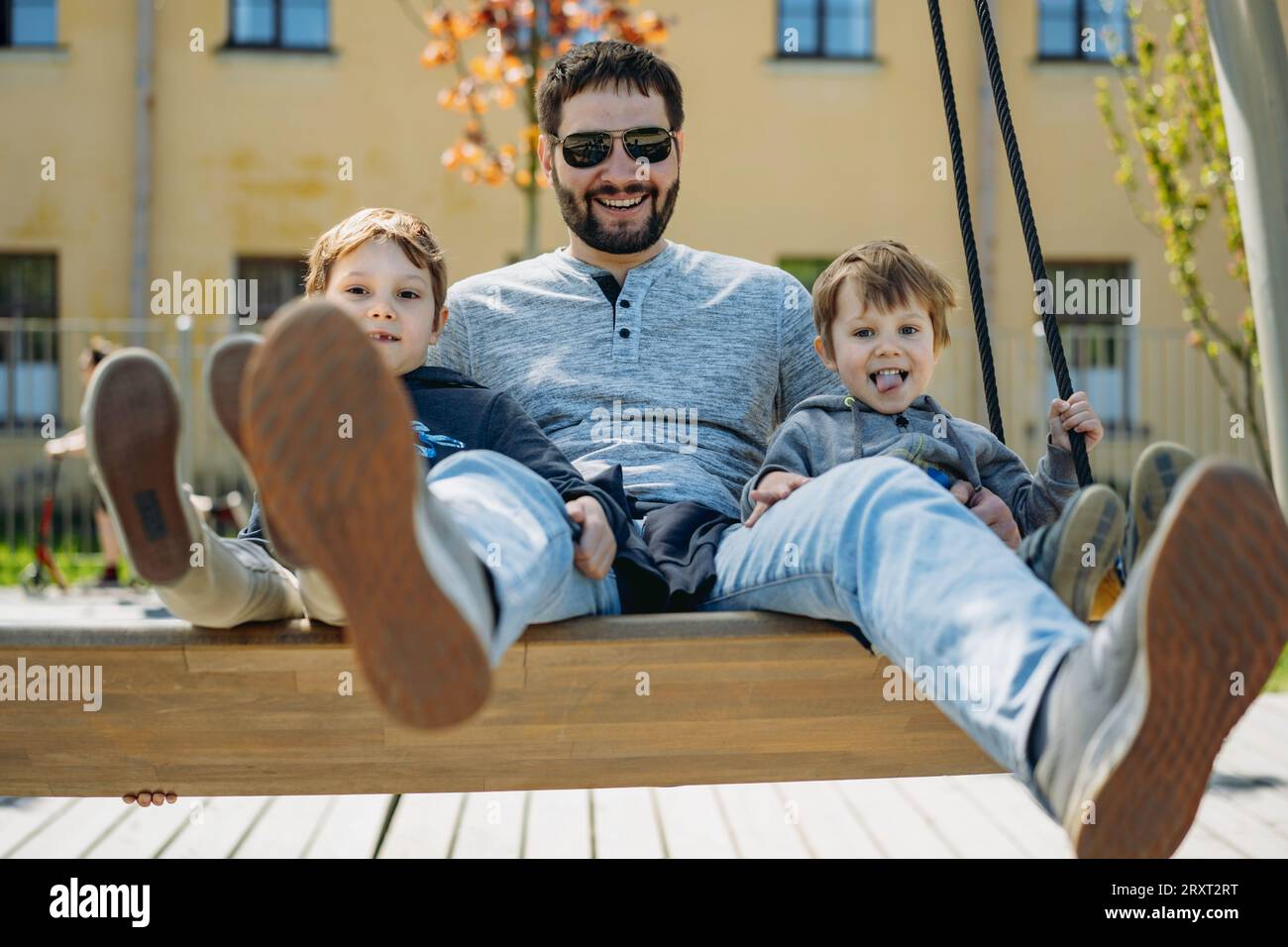 father with two sons swinging on bench swings together. Father nis ...