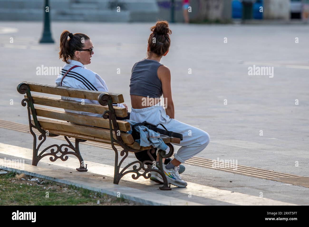 two young women sitting on a park bench chatting Stock Photo - Alamy