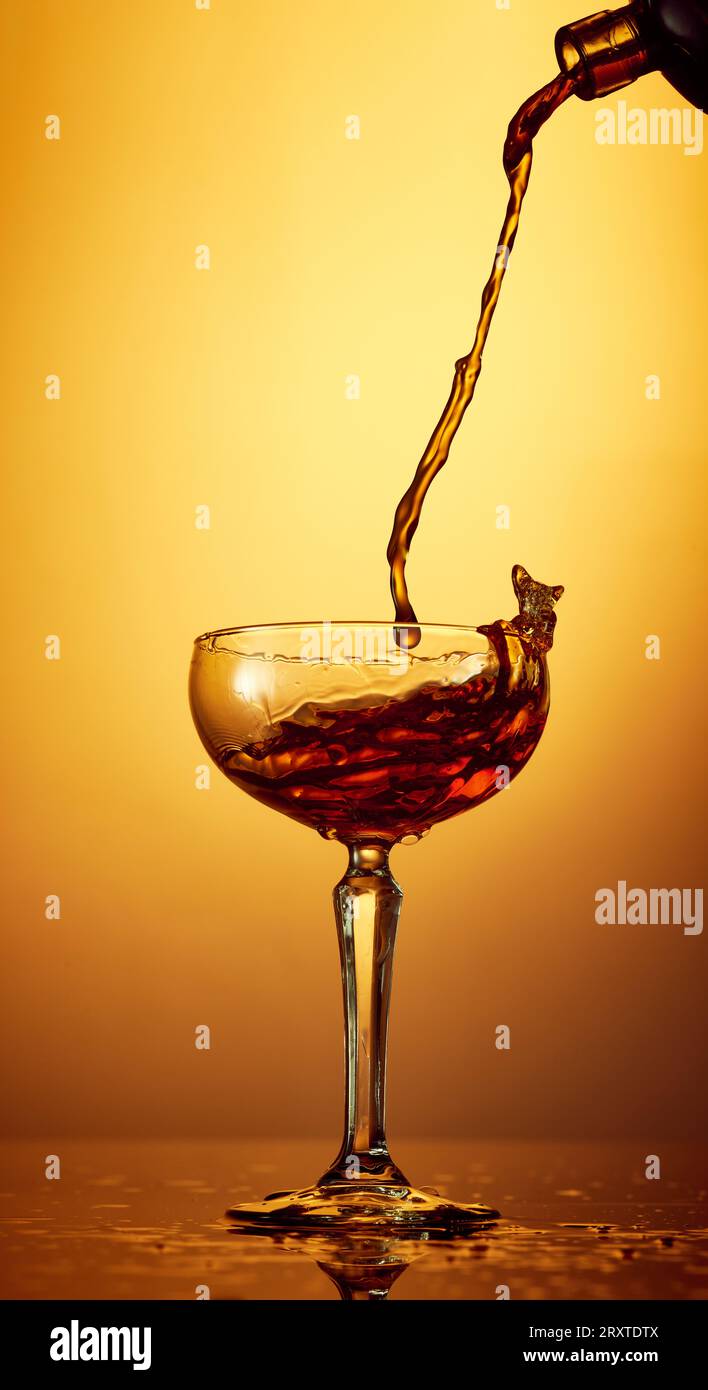 Photo of pouring whiskey, rum, brandy or gin to high glass with splash ...