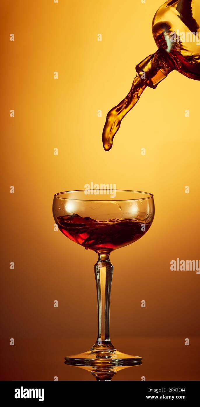 Photo of pouring whiskey, rum, brandy or gin from bottle to high glass ...