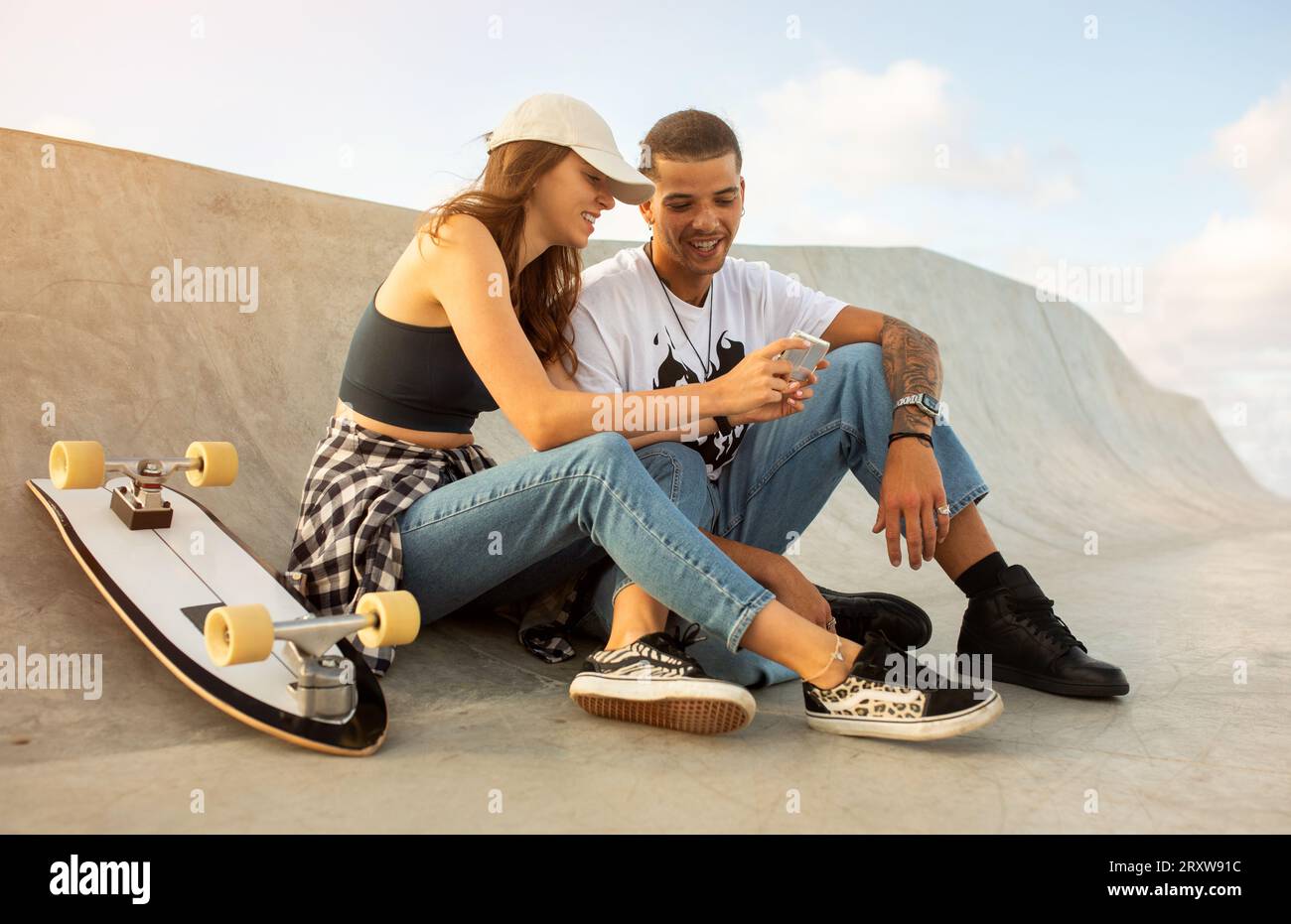 European couple sitting on skateboarding ramp, using phone and surfing ...