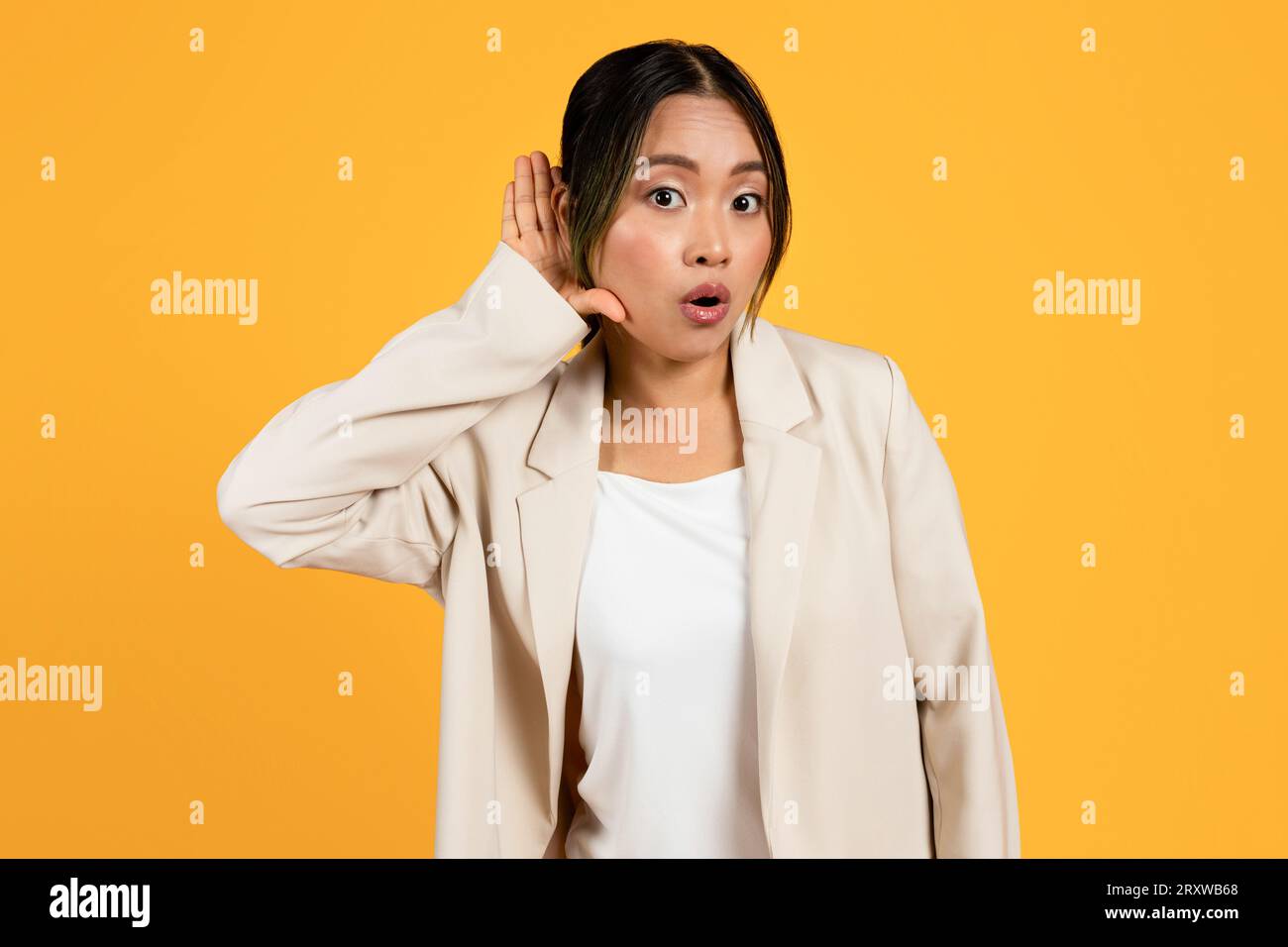 Shocked curious young asian woman in suit, put hand to ear, listening ...