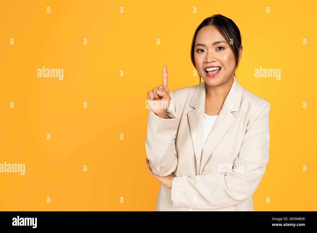 Positive young asian woman in suit point finger up at free space ...