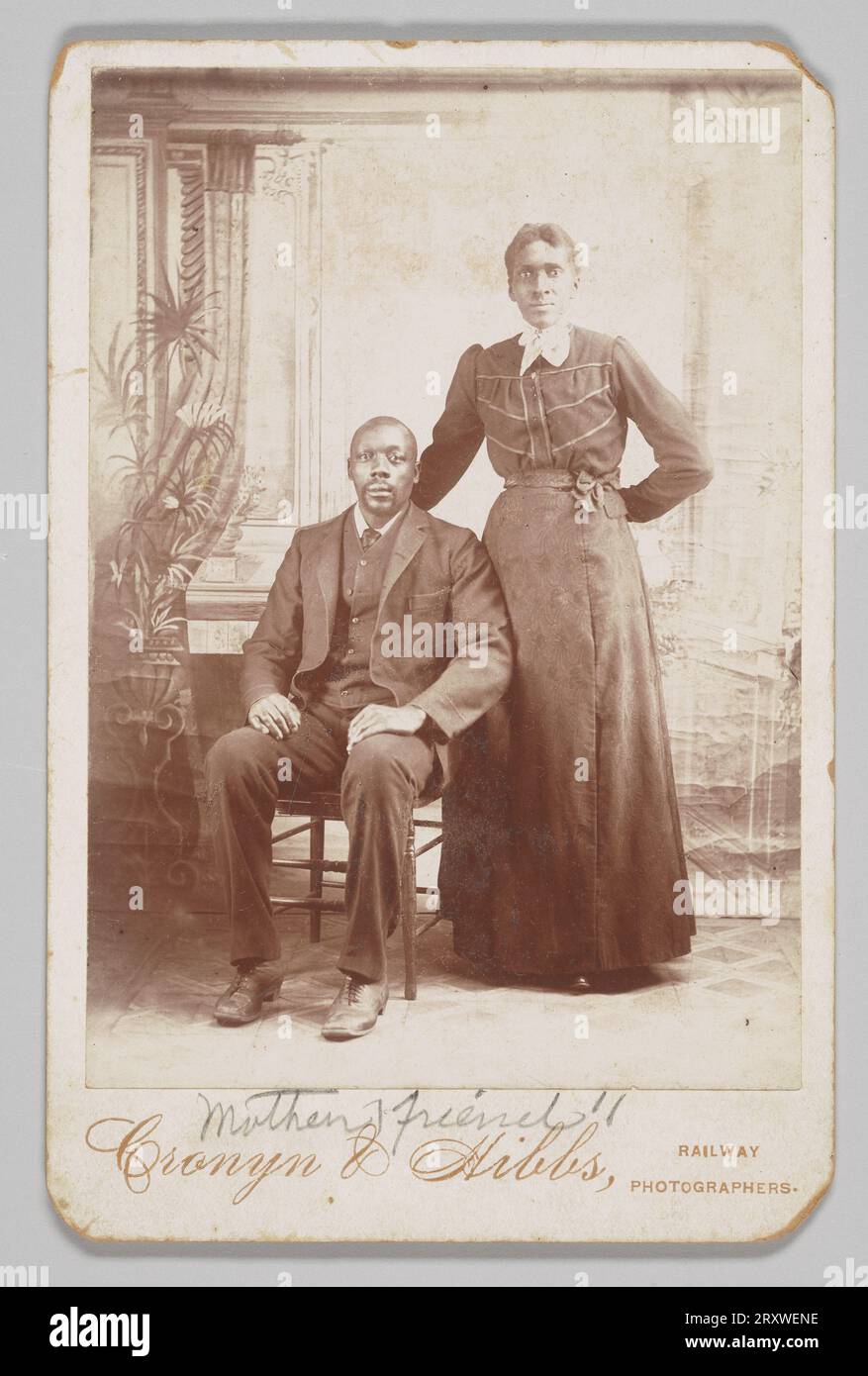 Photograph of a man sitting down with a woman standing next to him ...